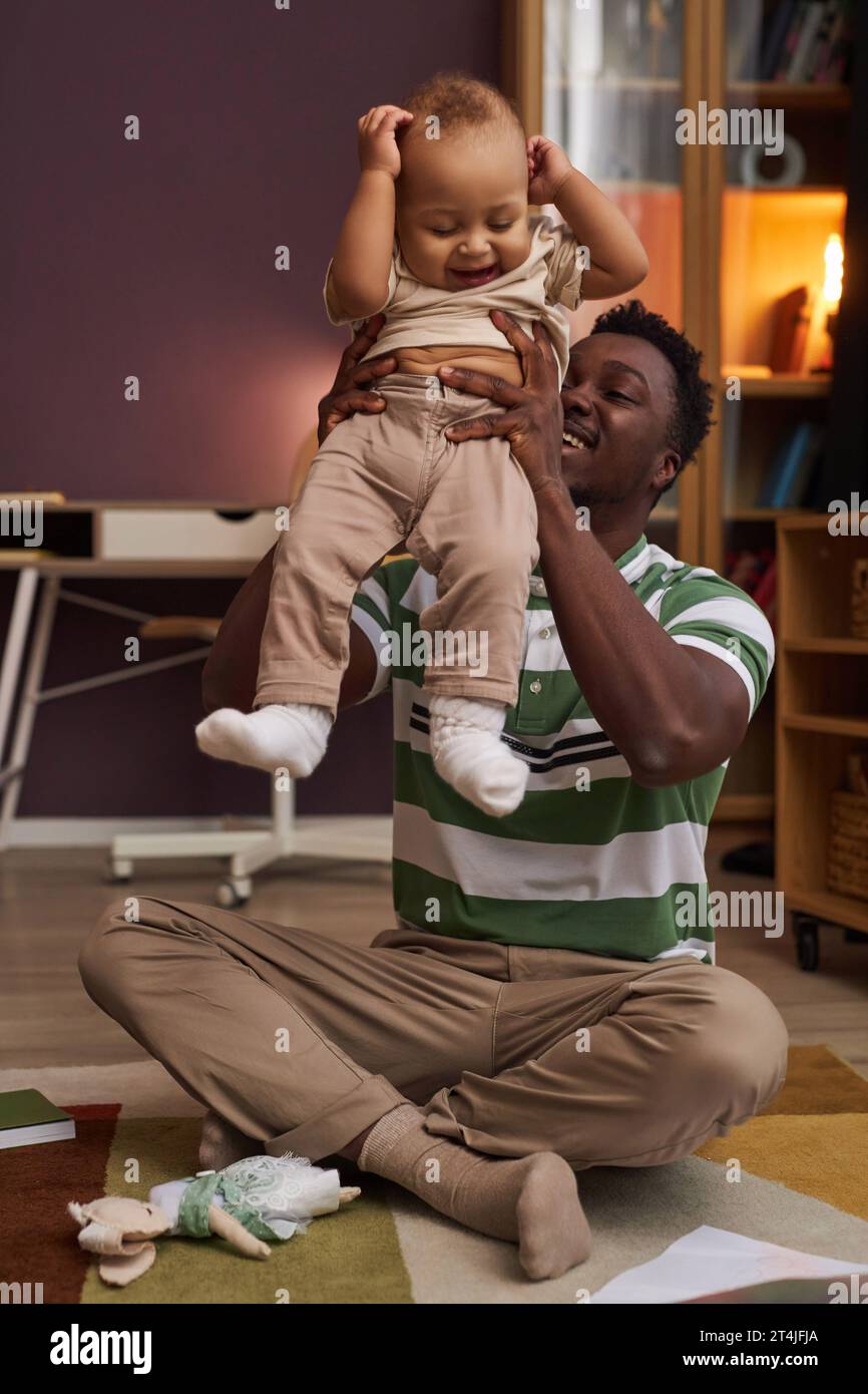 Vertical full length portrait of happy Black father playing with baby ...