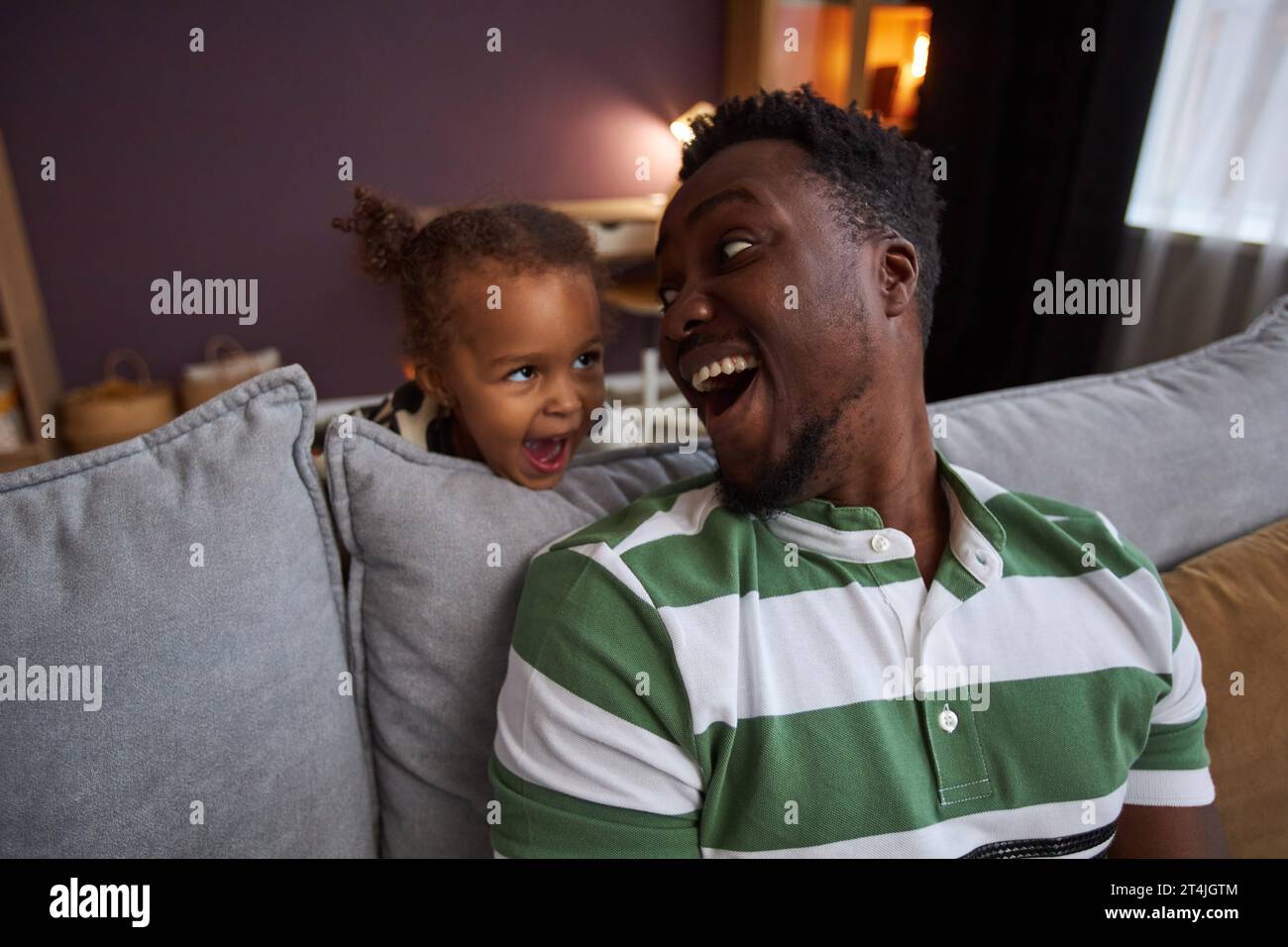 Portrait of cute Black girl playing hide and seek with father at home ...
