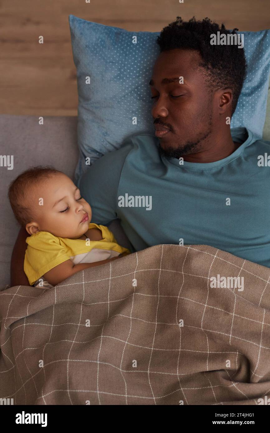 Top down view of exhausted Black man as father sleeping with cute baby ...