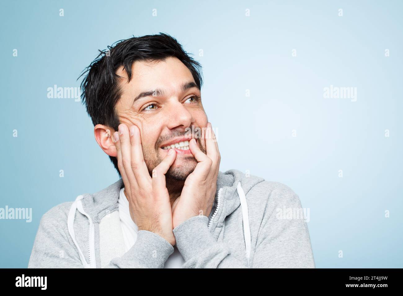 Thinking of silly things. a young man touching his face against a ...
