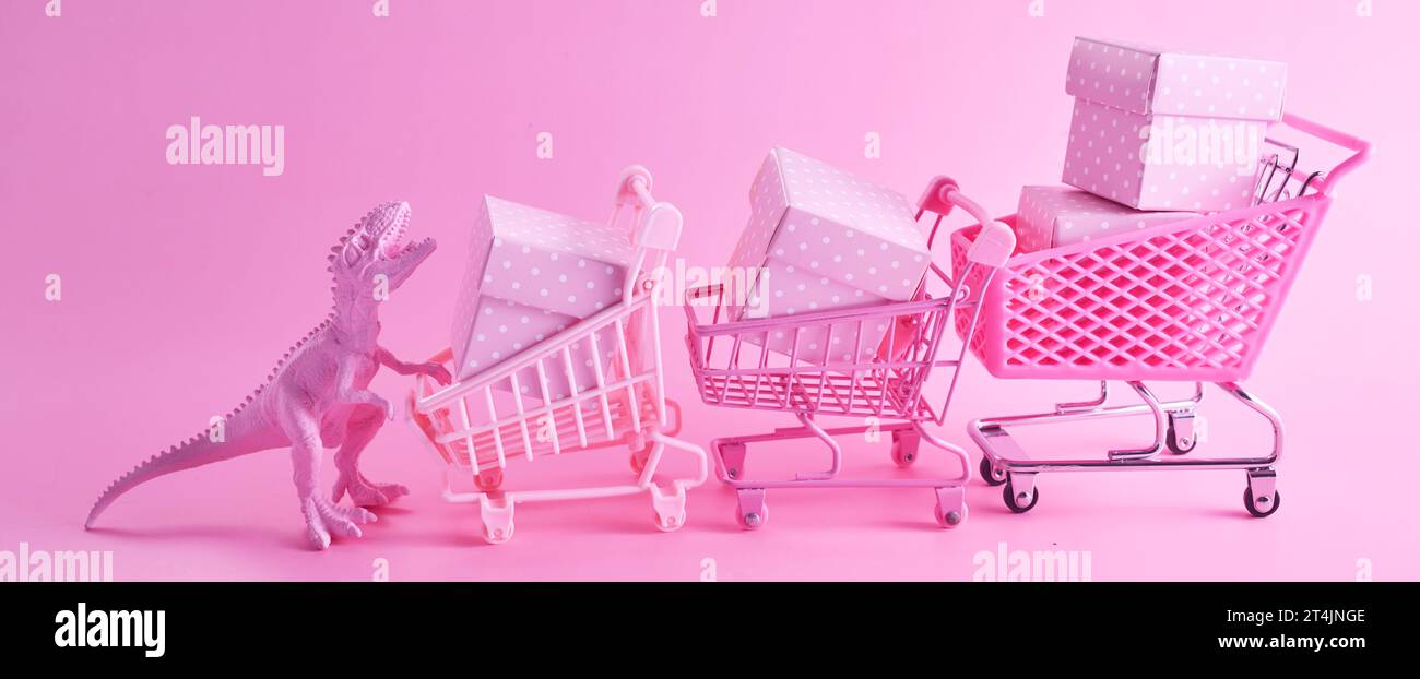 Pink Friday concept. Funny pink dinosaur toy with shopping cart full of ...
