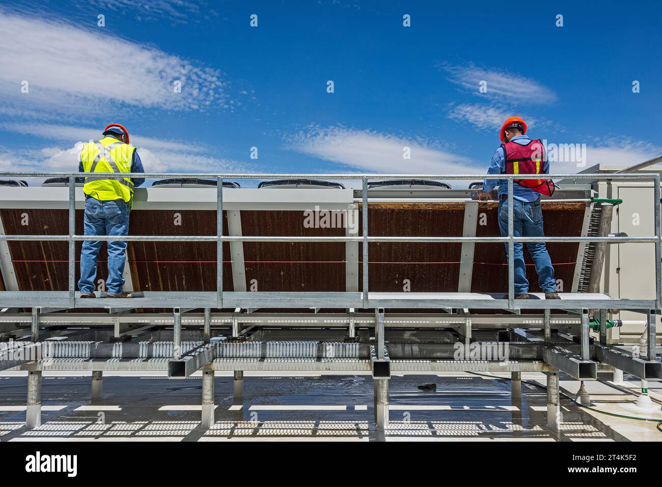 Two construction workers work on an adiabatic condenser on the roof at ...