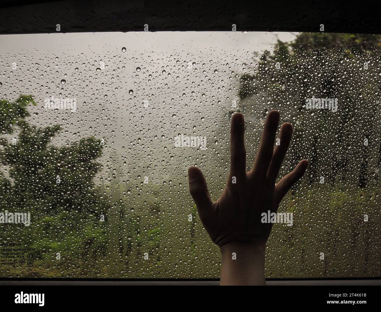 Silhouette of hand on glass with water drops in lonely rainy day. Close ...