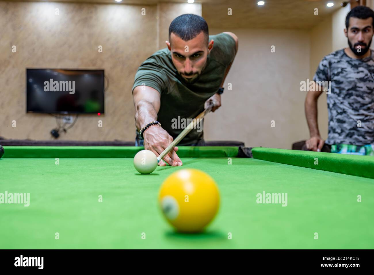 Young adult bearder male playing billiards with his friends focusing on ...
