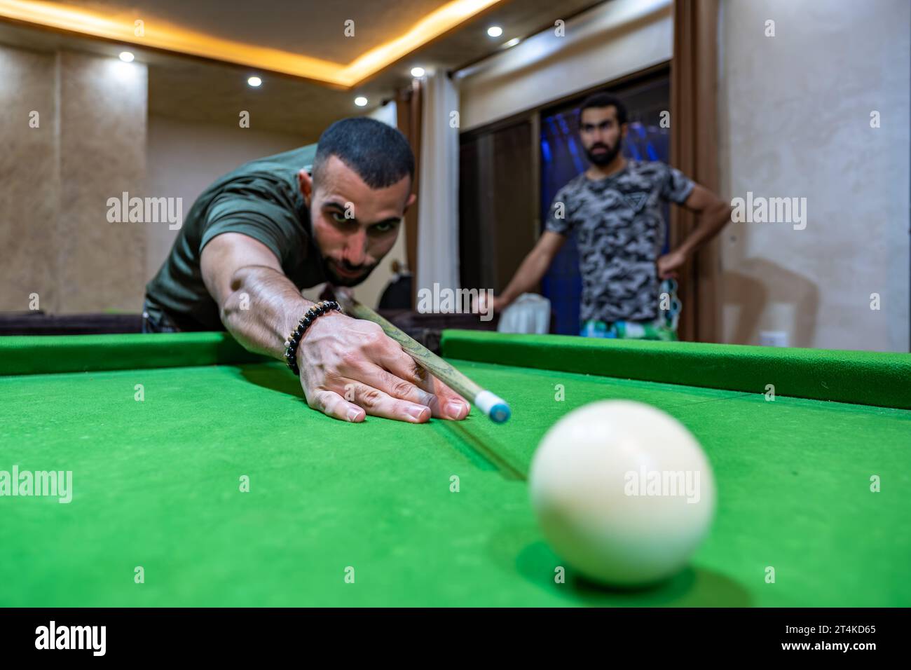 Young adult bearder male playing billiards with his friends focusing on ...