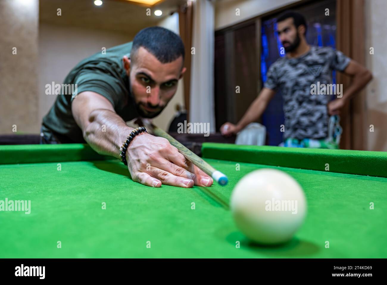 Young adult bearder male playing billiards with his friends focusing on ...