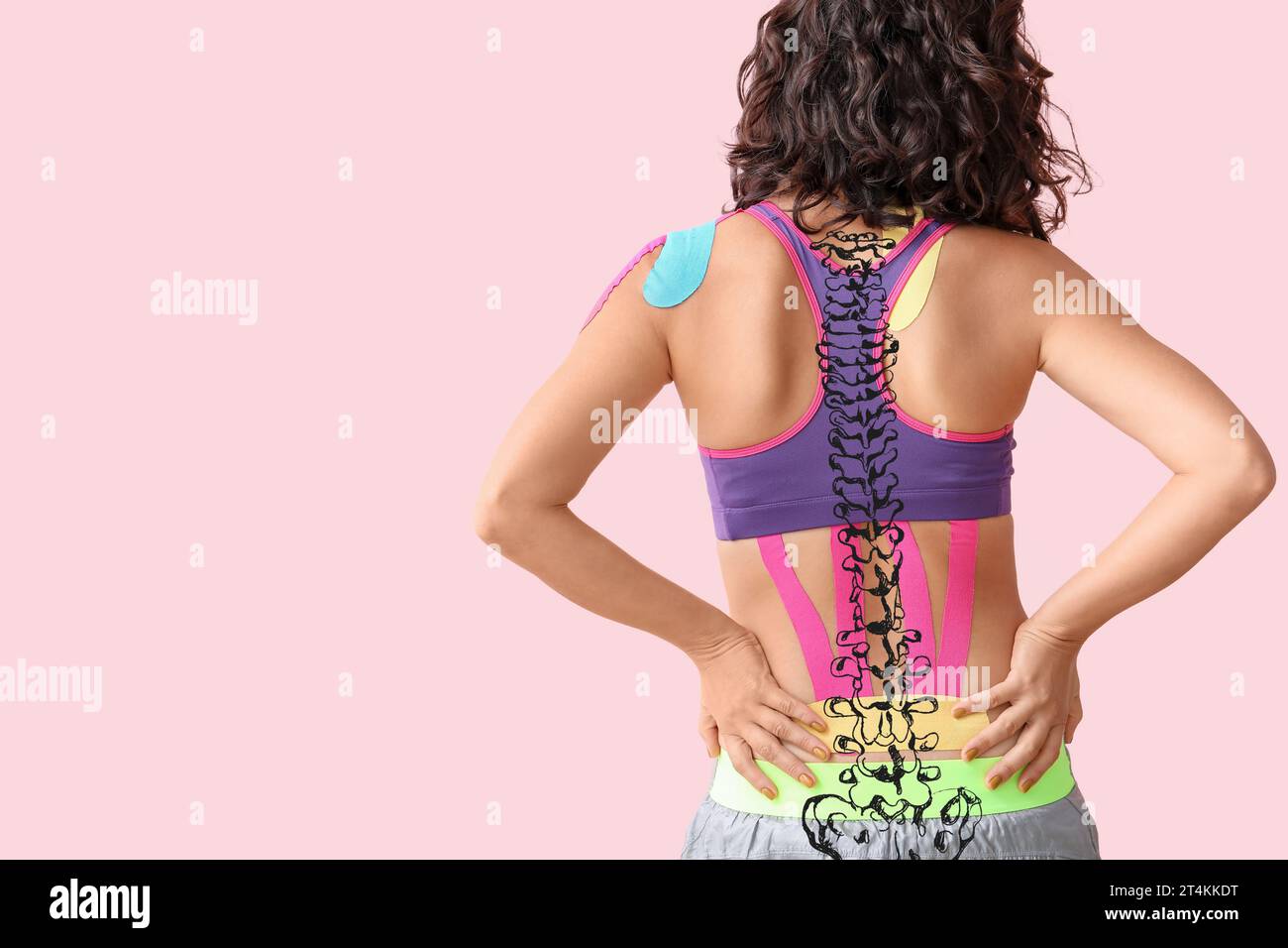 Sporty woman with physio tape applied on her back against pink ...