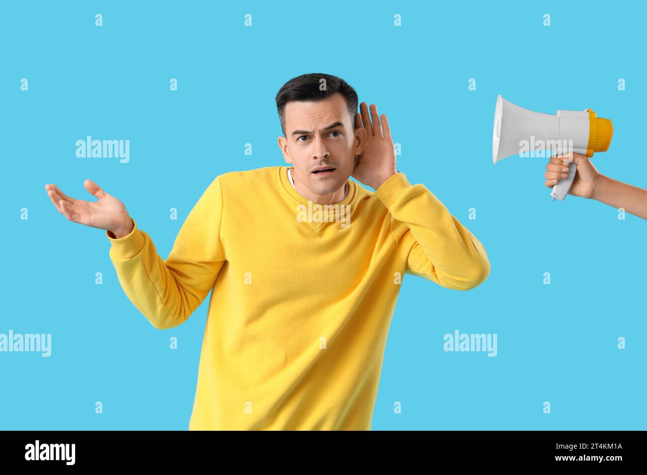Young man trying to hear something and hand with megaphone on blue ...