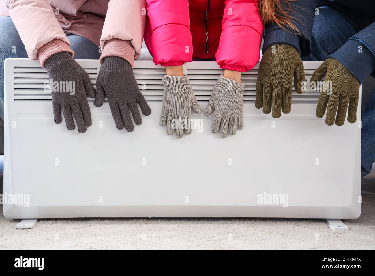 Frozen family in winter clothes warming near radiator at home, closeup ...
