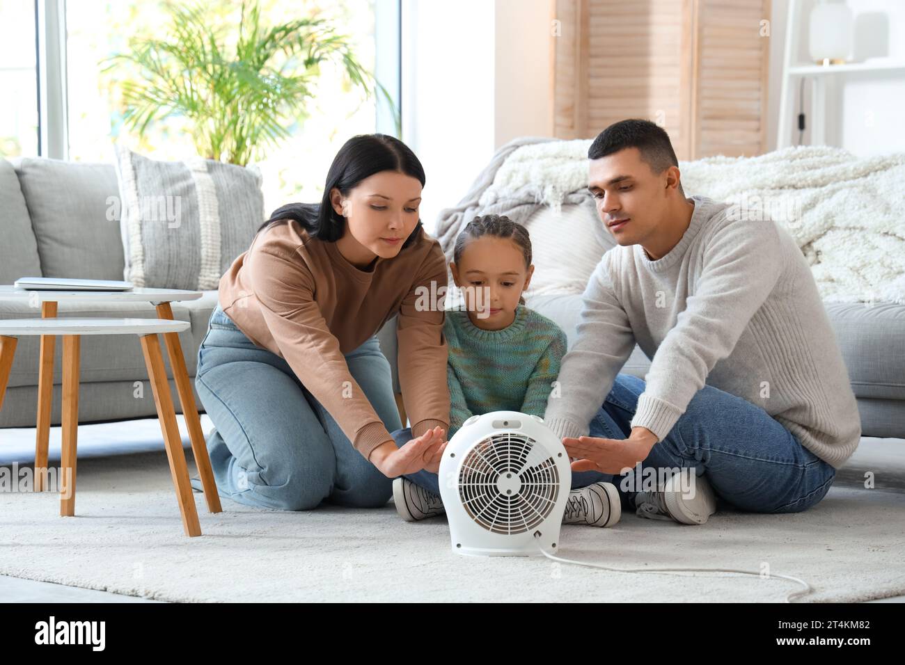 Frozen family warming near electric fan heater at home Stock Photo - Alamy