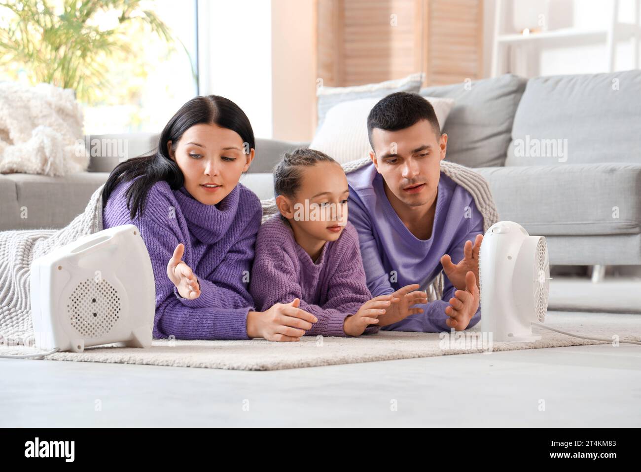 Frozen family warming near electric fan heaters at home Stock Photo - Alamy