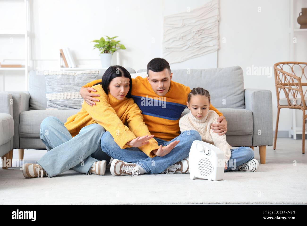 Frozen family warming near electric fan heater at home Stock Photo - Alamy