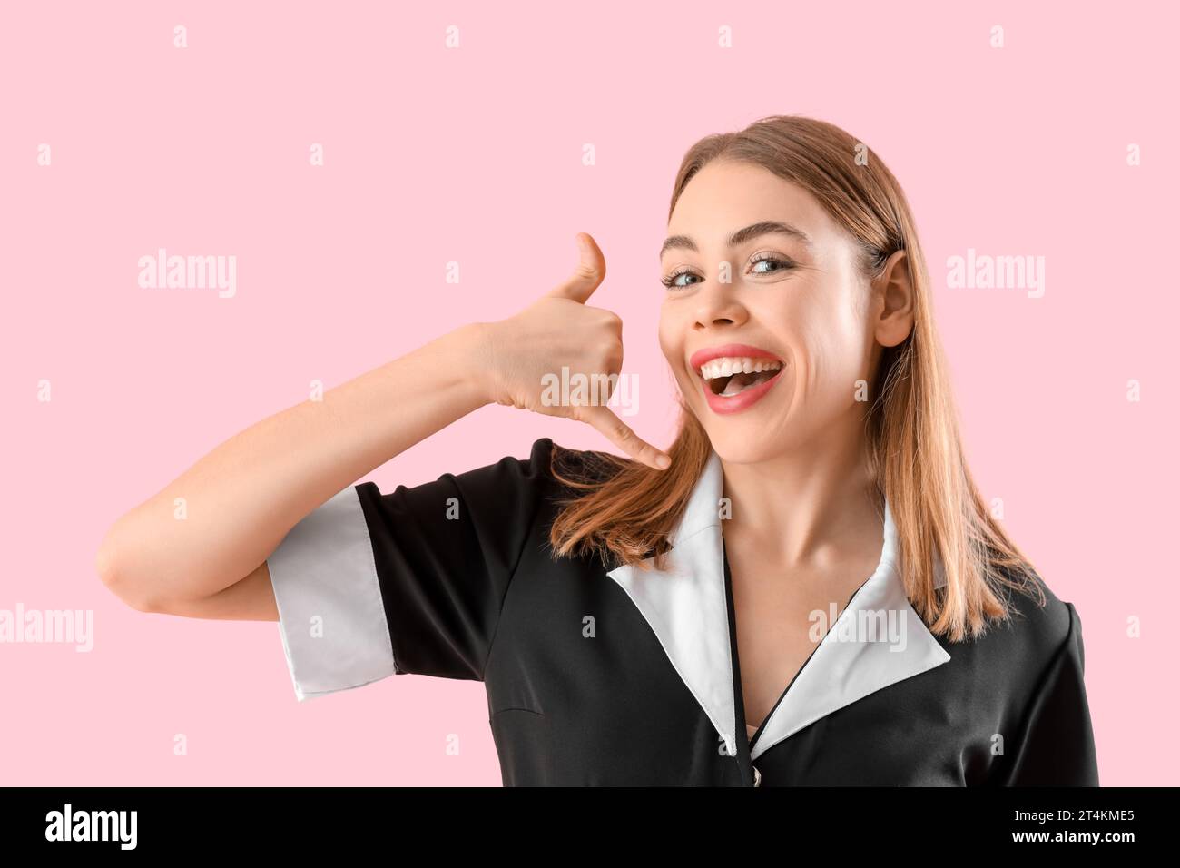 Beautiful female janitor showing "call me" gesture on pink background ...