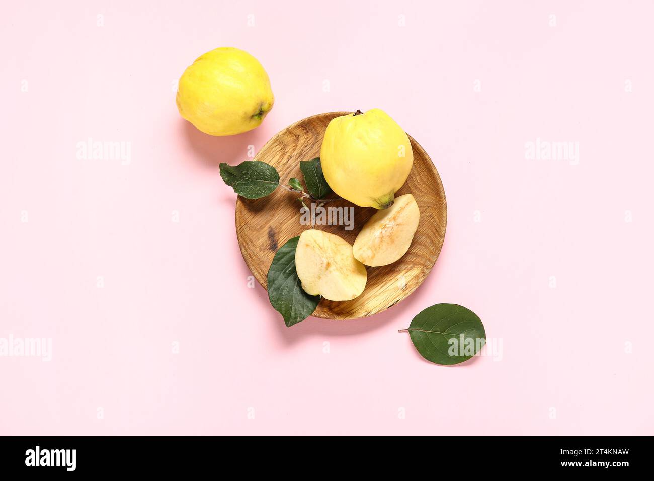 Wooden plate with sweet ripe quinces and leaves on pink background ...