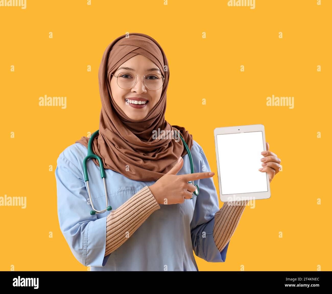 Muslim medical intern with tablet computer on yellow background Stock ...