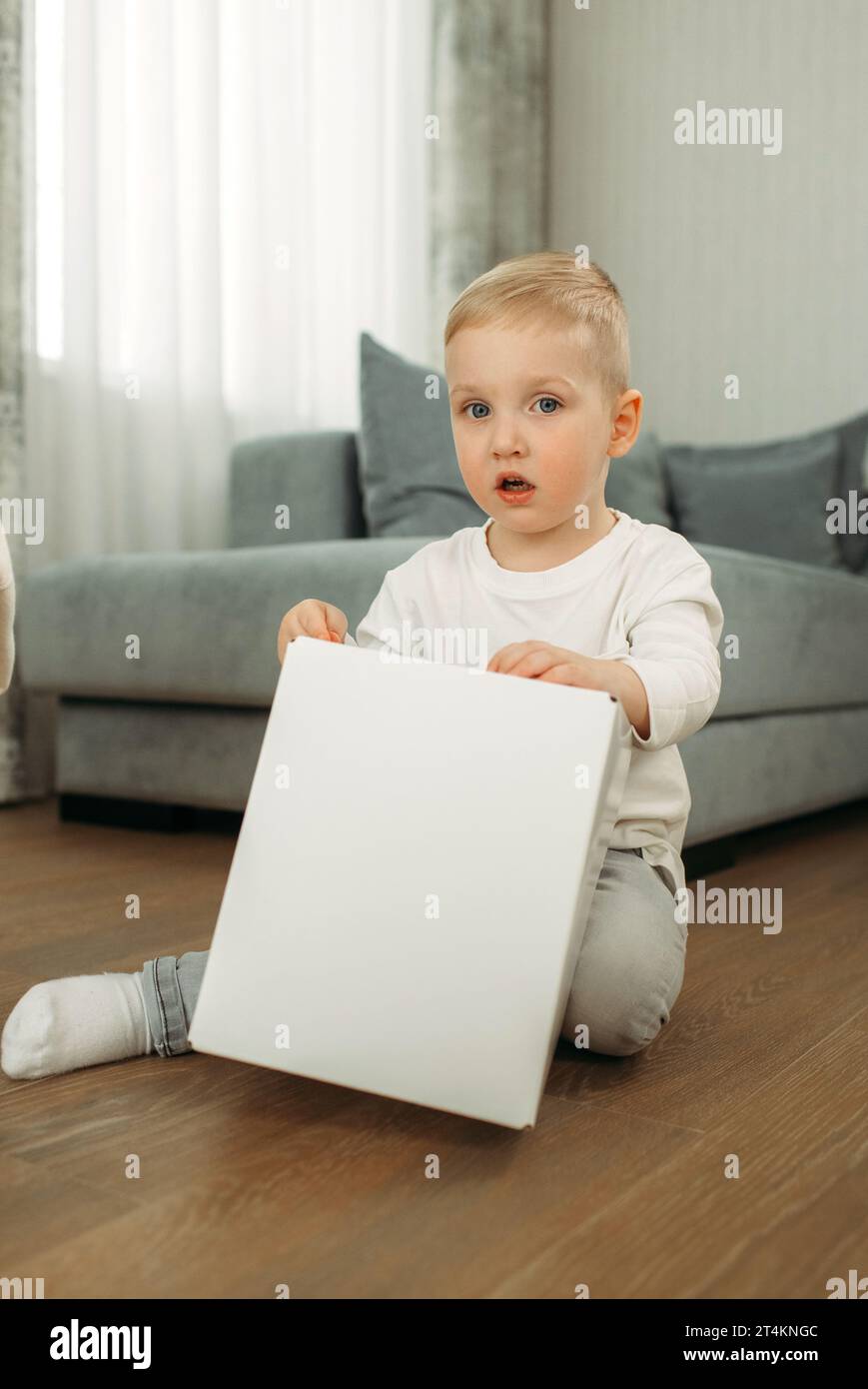 A child sits on the floor with a cardboard box. Playing. Boy holding a ...