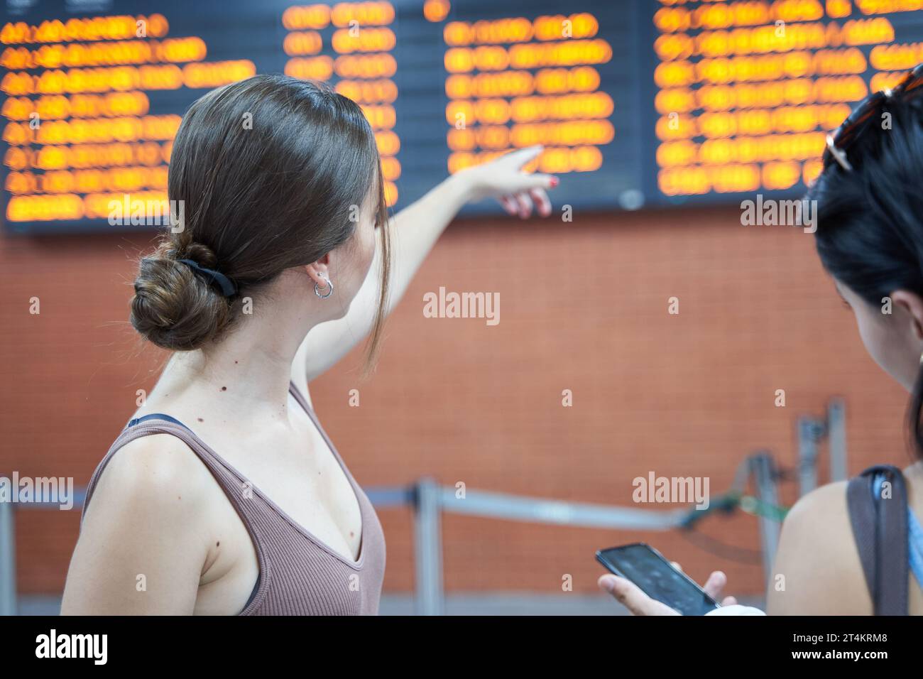 Back view of couple in airport, looking and pointing at travel board ...