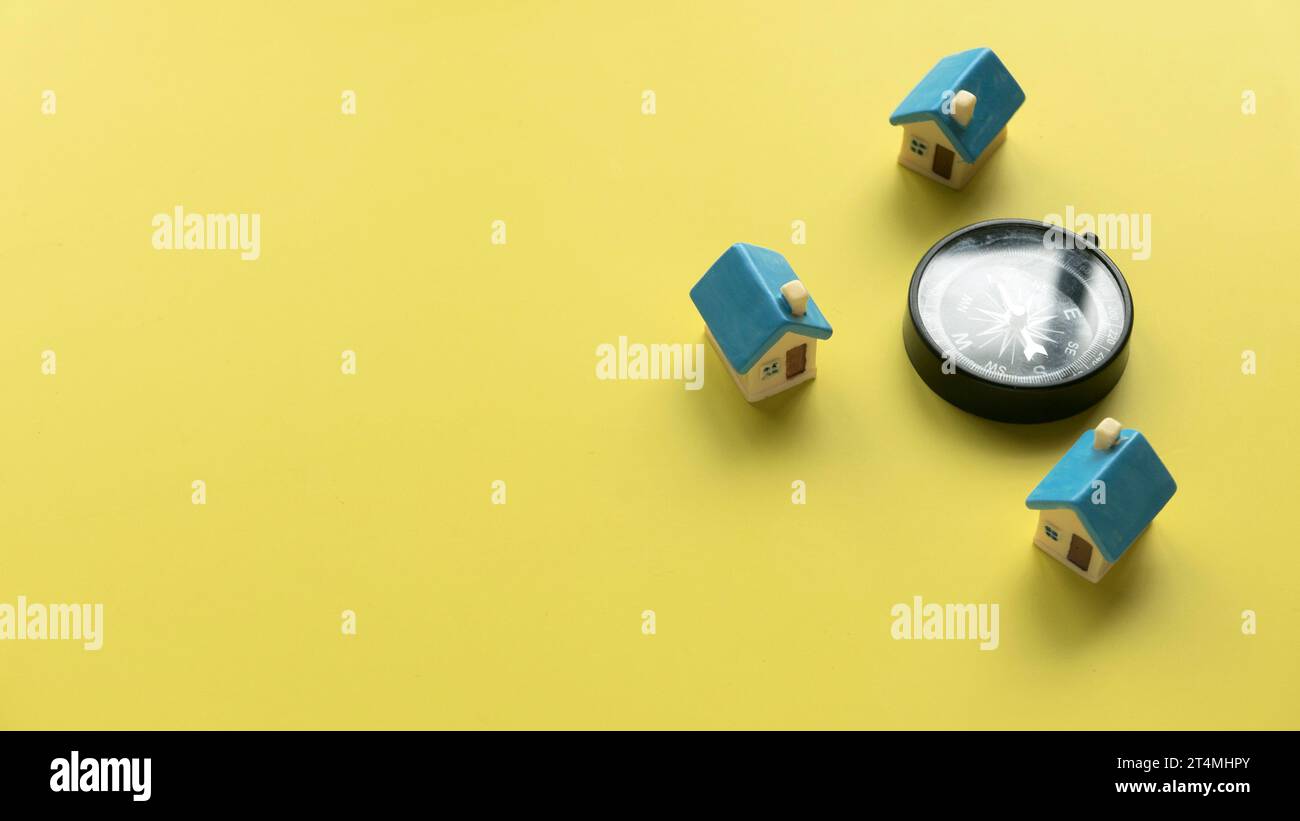 Miniature house and a compass over a yellow background with copy space ...
