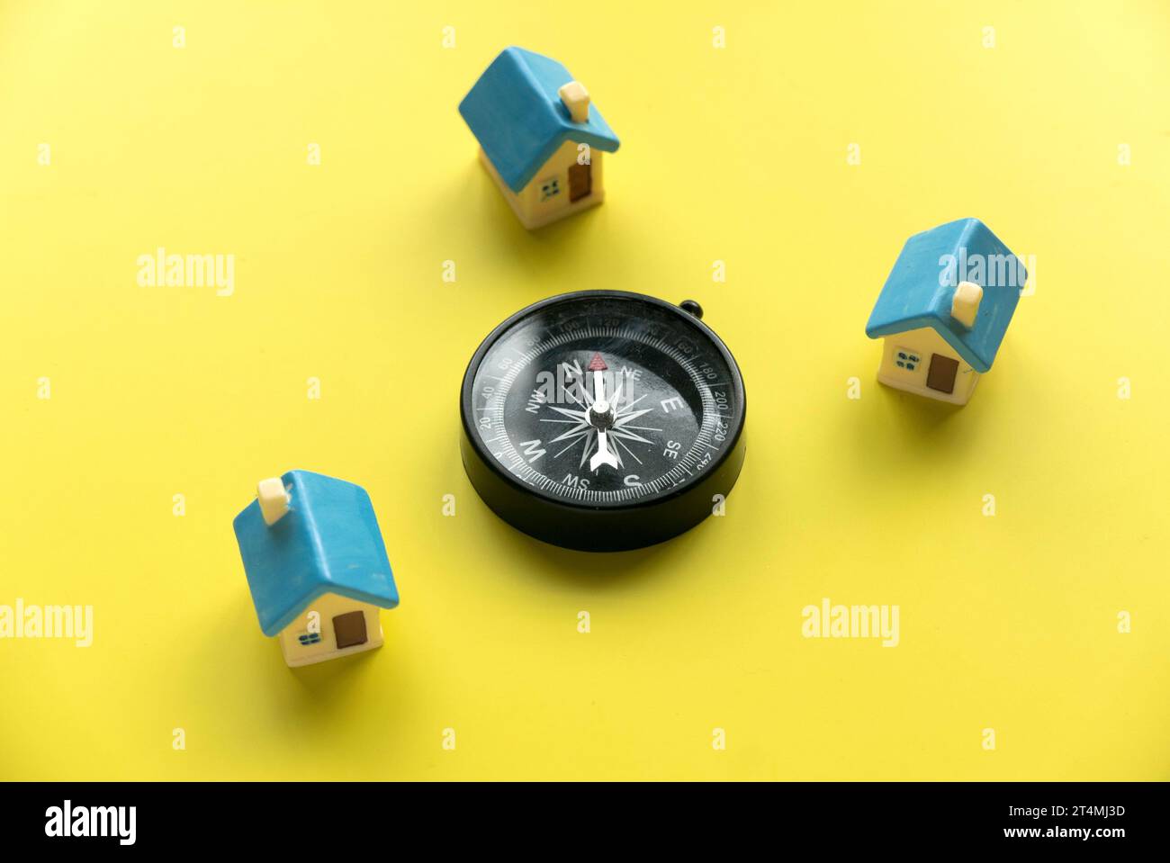 Miniature house and a compass over a yellow background Stock Photo - Alamy