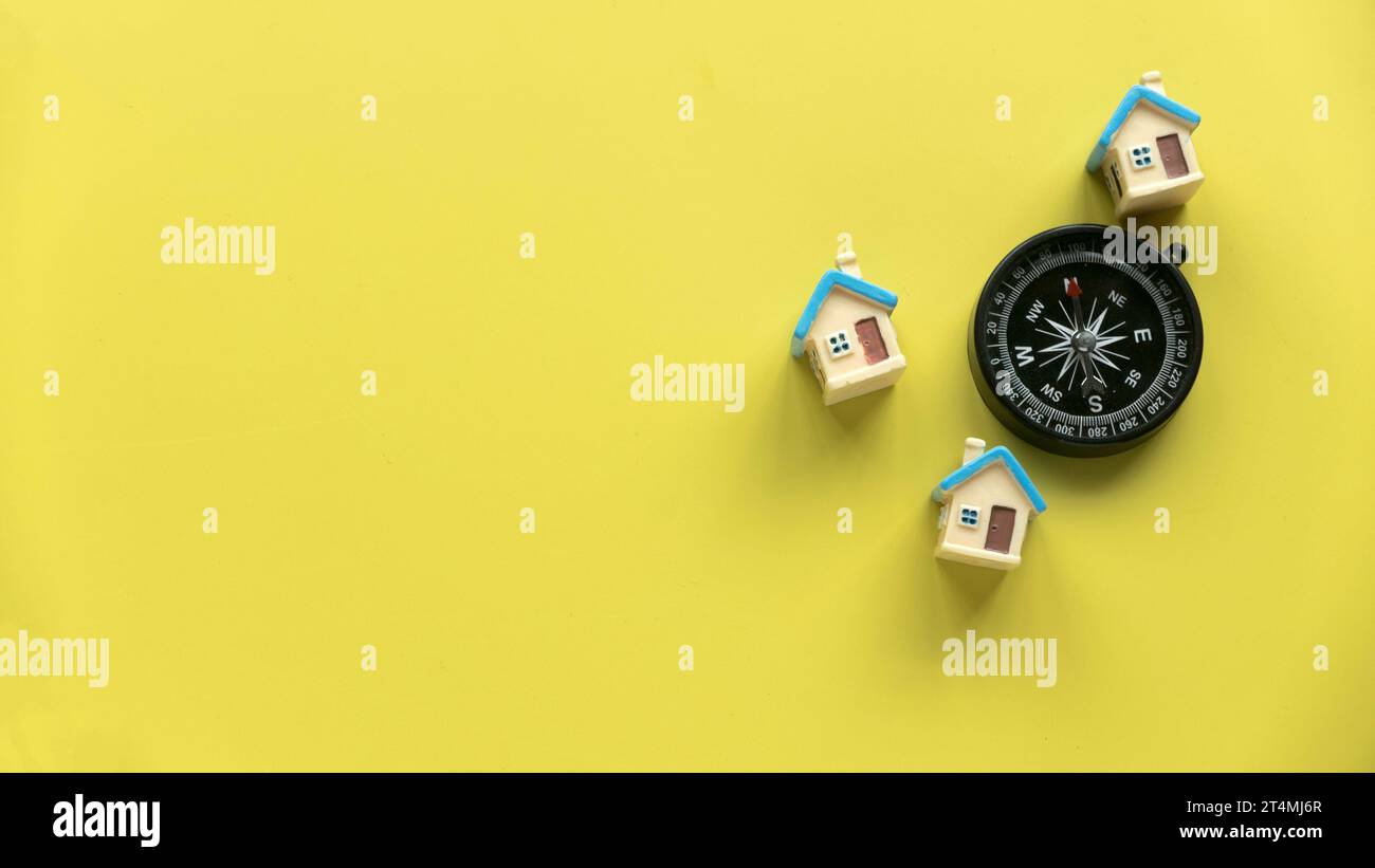 Miniature house and a compass over a yellow background with copy space ...