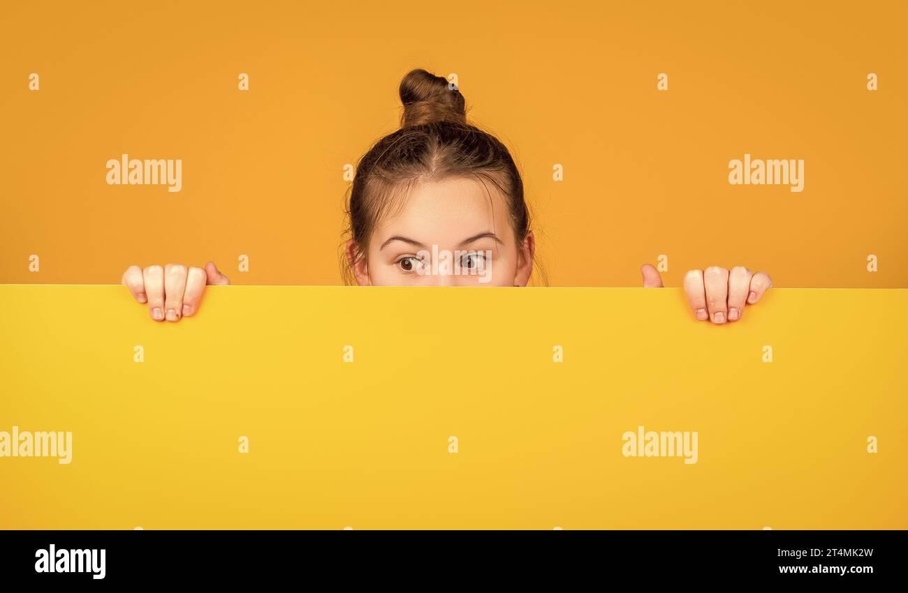kid hiding behind blank yellow paper with copy space for advertisement ...