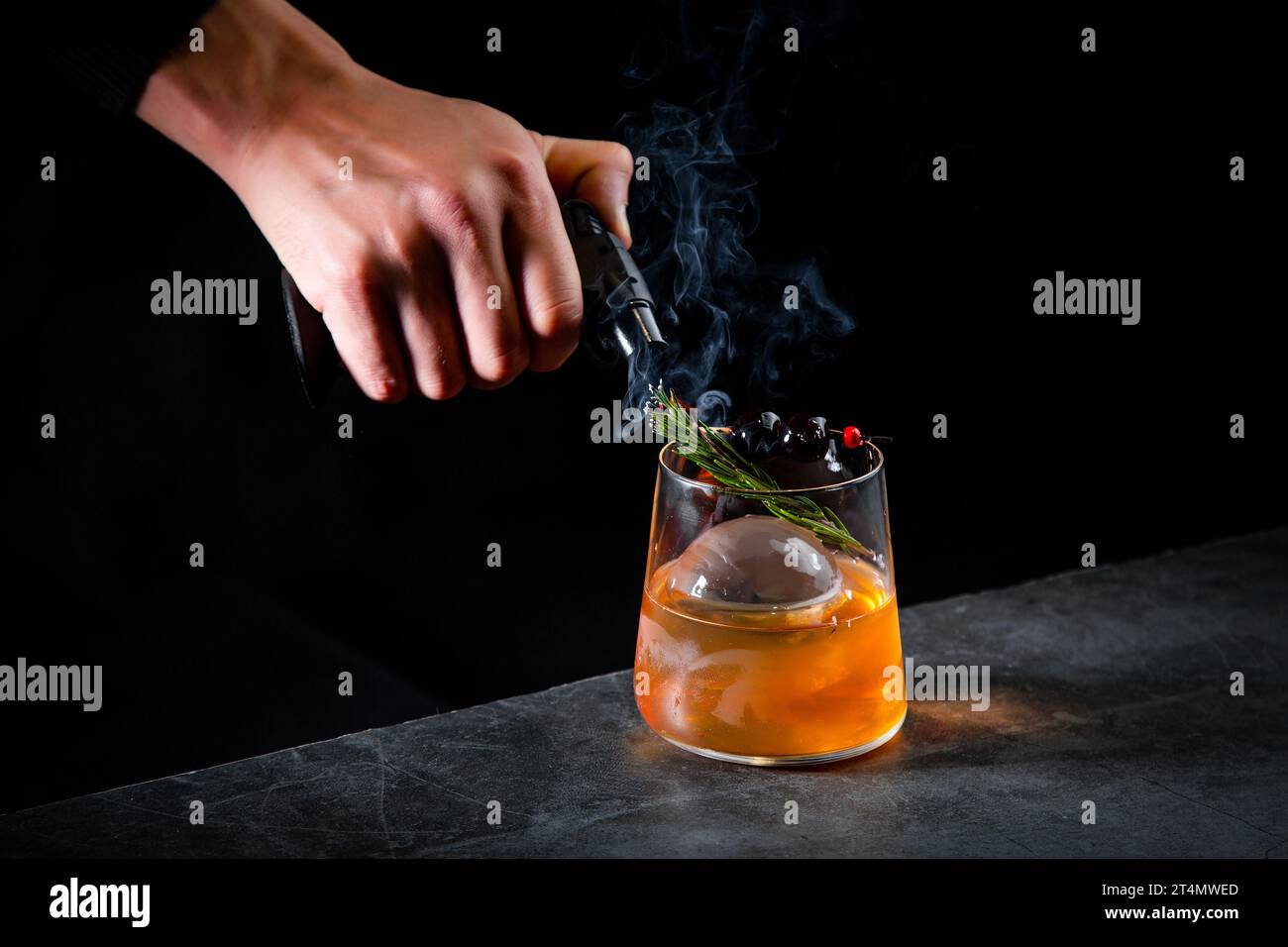 orange alcoholic cocktail with a sprig of pine needles and round ice ...