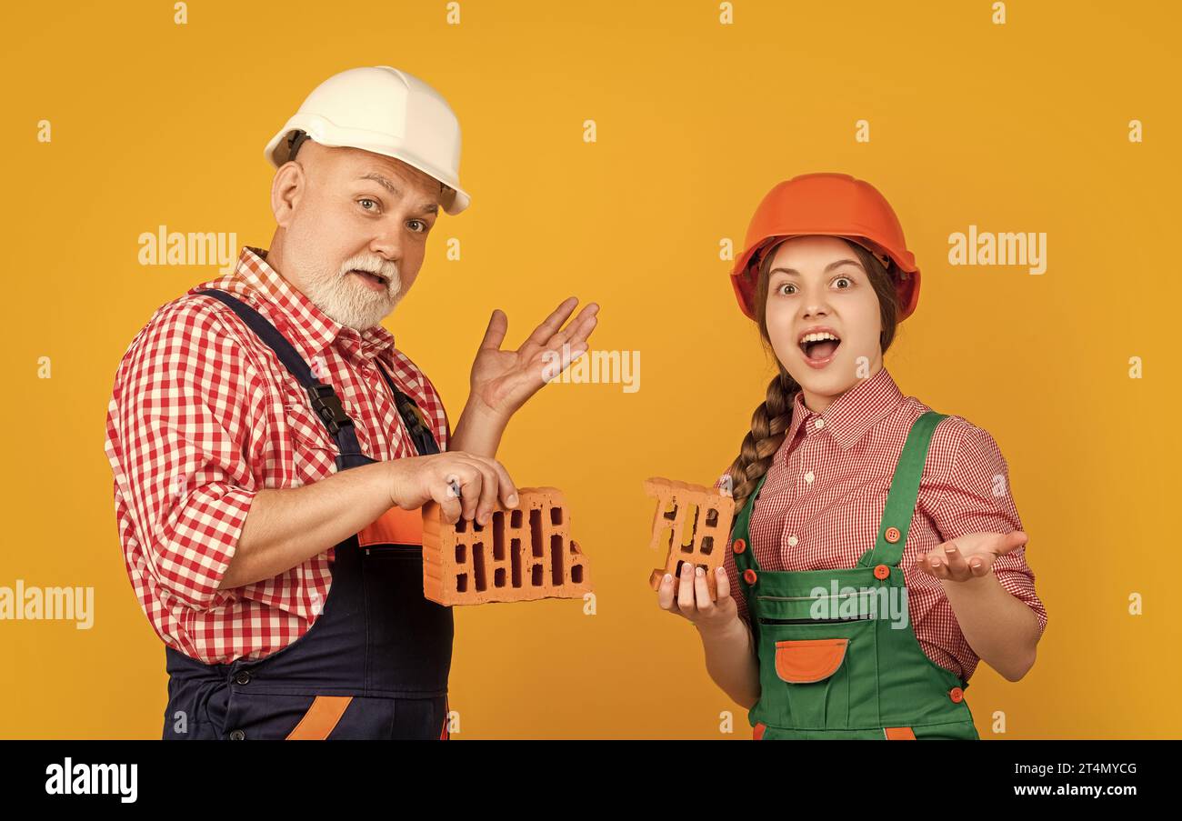 amazed child and grandfather bricklayer in helmet on yellow background ...