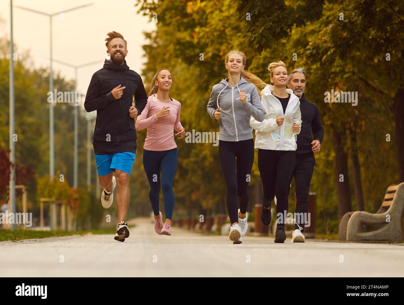 Healthy group of smiling people jogging along a path in the park having ...