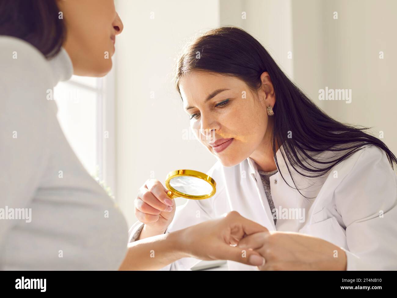Female doctor examining hand skin of a young woman patient using ...