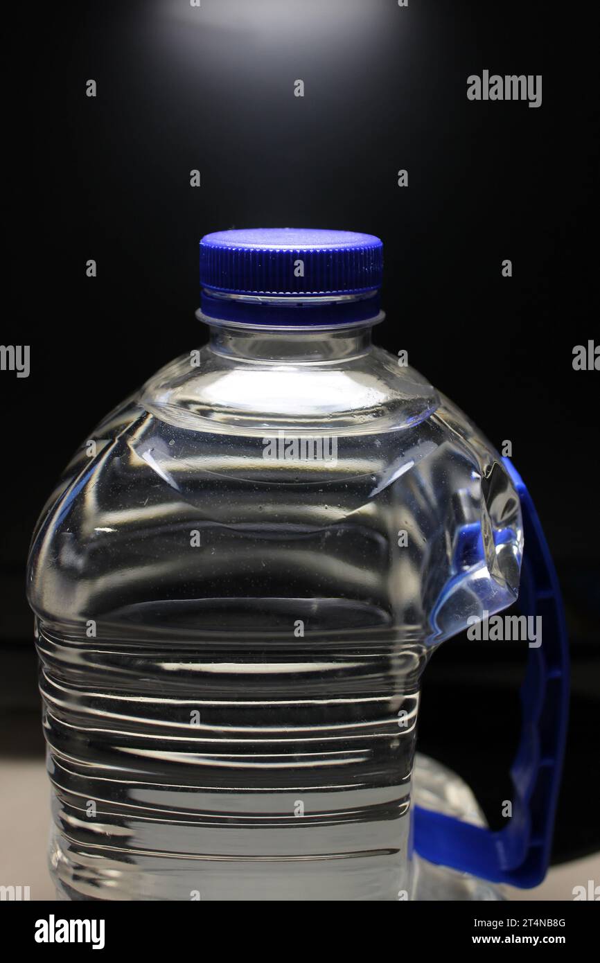 A large bottle with a plastic handle filled with clean water over black ...