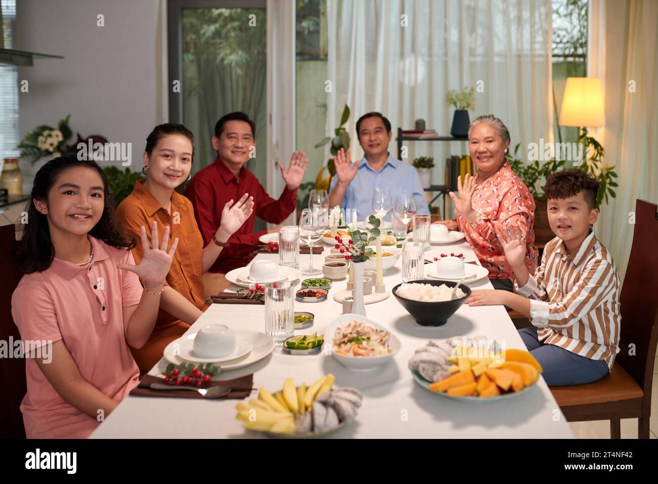 Big Vietnamese family sitting at dinner table and waving at camera ...