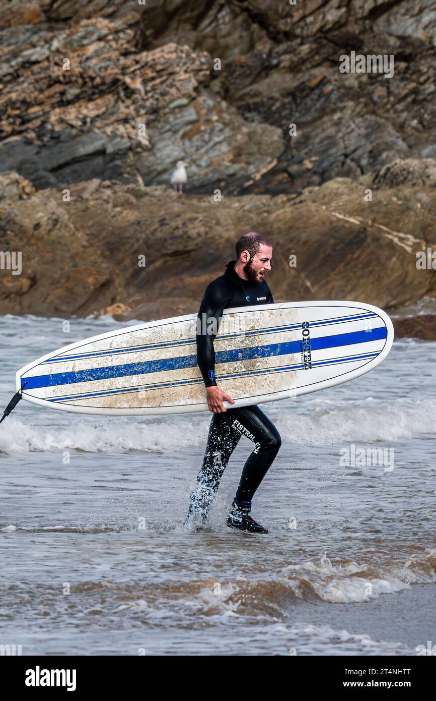 A tired male surfer carrying his surfboard after a surfing session at ...