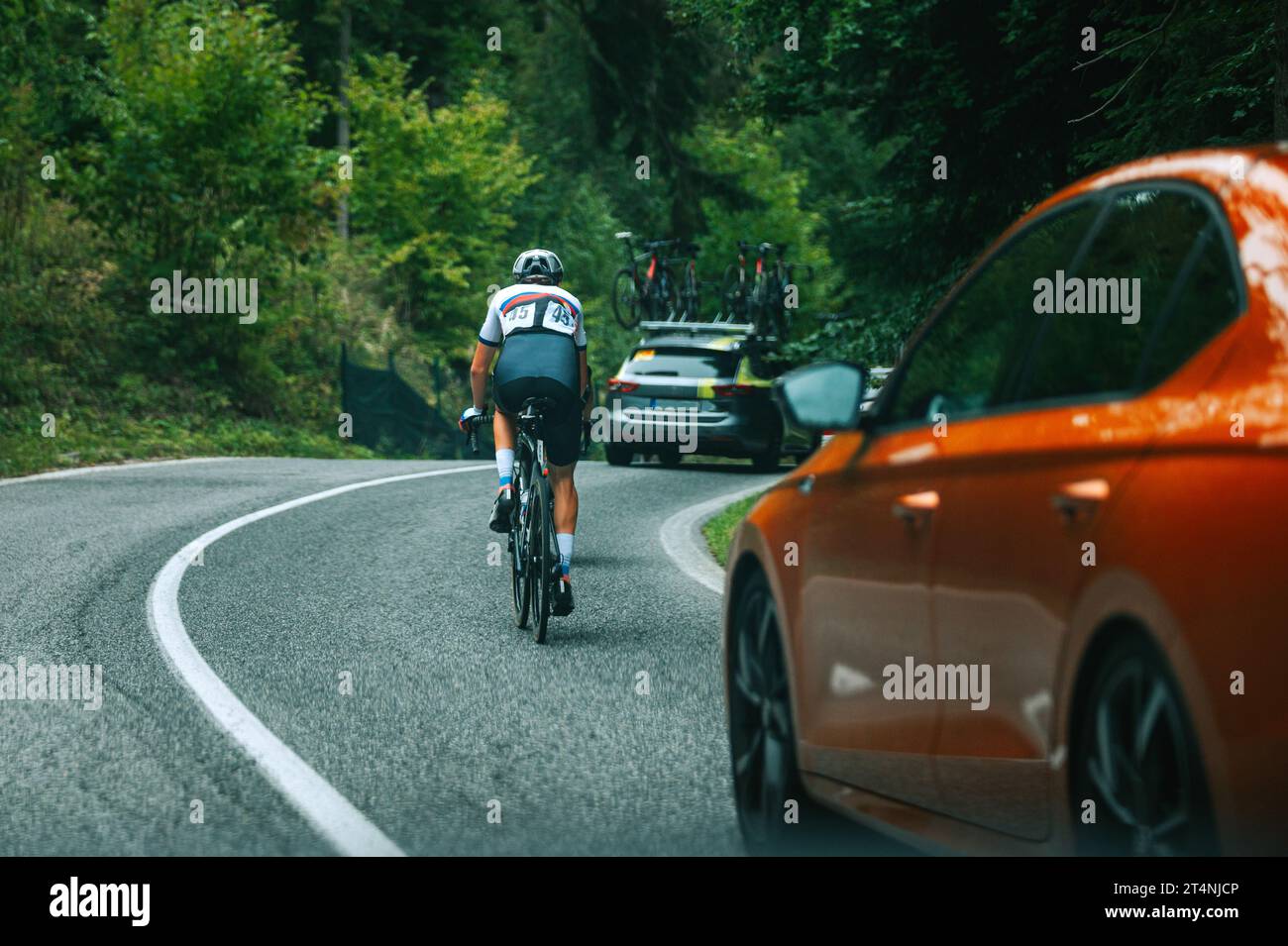 Alone cyclist behind the peloton riding between convoy of cars. Photo ...