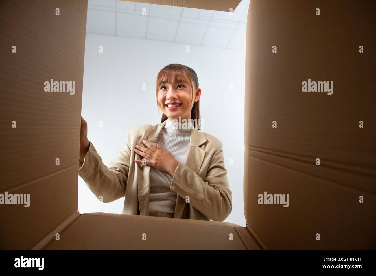 Young beautiful girl, opens and peeks into cardboard box. Bottom view ...