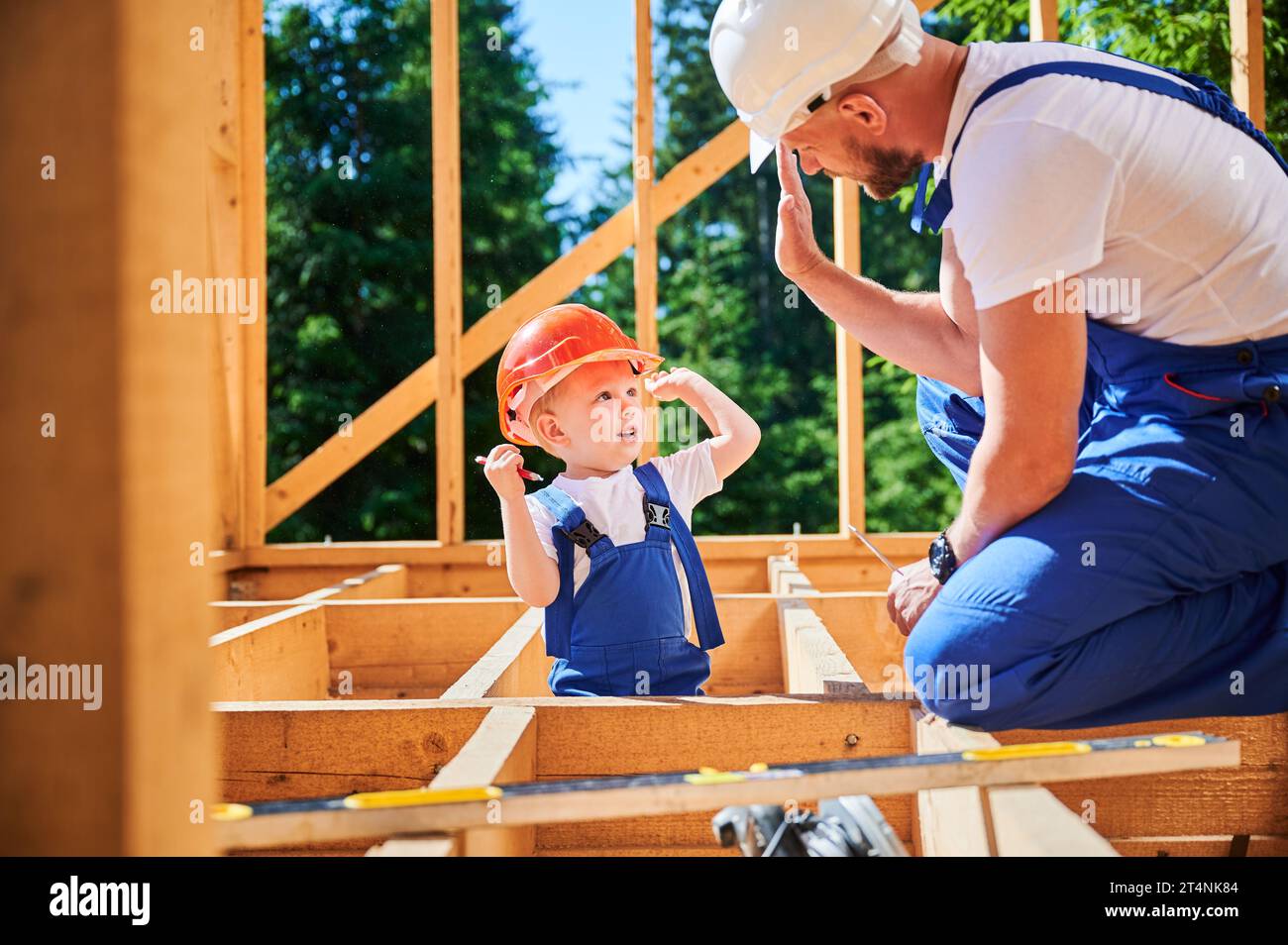 Father with toddler son building wooden frame house. Male worker giving ...