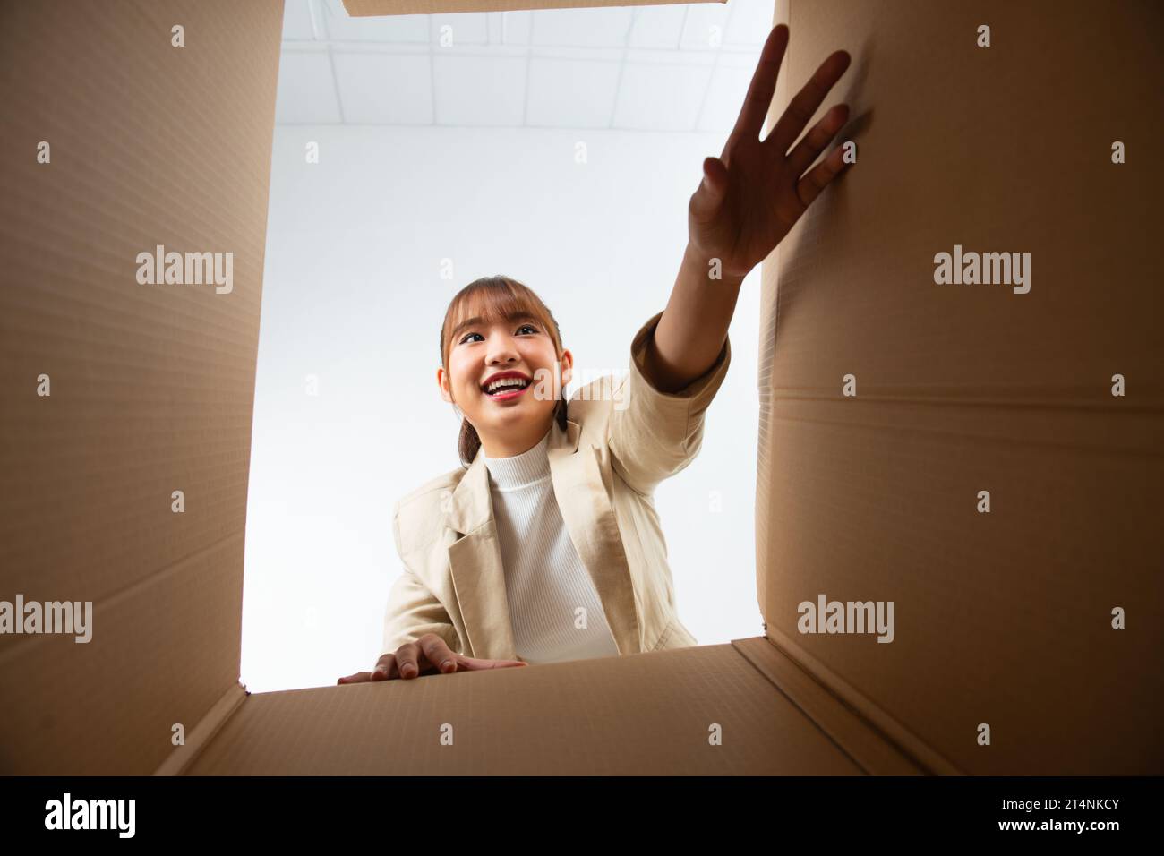 Smiling young woman opening a carton box, relocation and unpacking ...