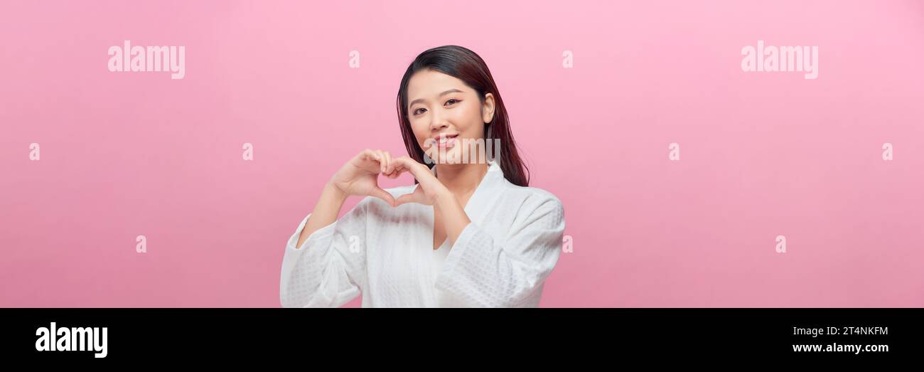 happy smiling young woman making hand heart gesture over pink ...