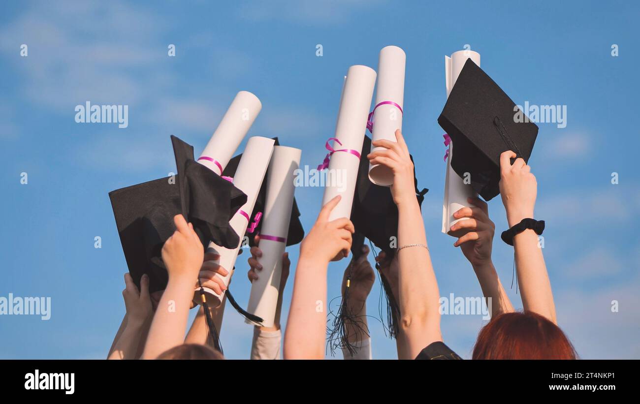College graduates raise their hands with caps and diplomas to the sky ...