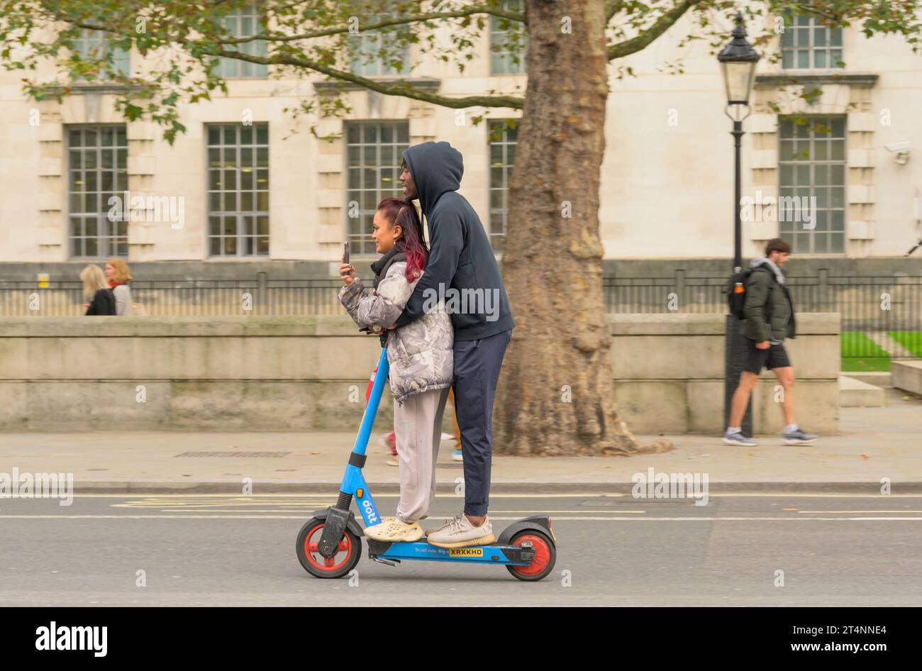 London, UK. Two young people sharing an e-scooter and filming on a ...