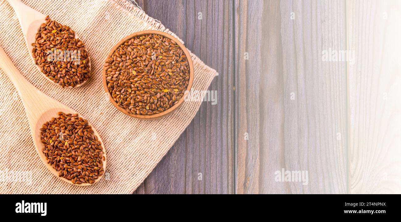 Brown flax seeds or flax seed in a small bowl on sacking and two wooden false on a brown wooden ...