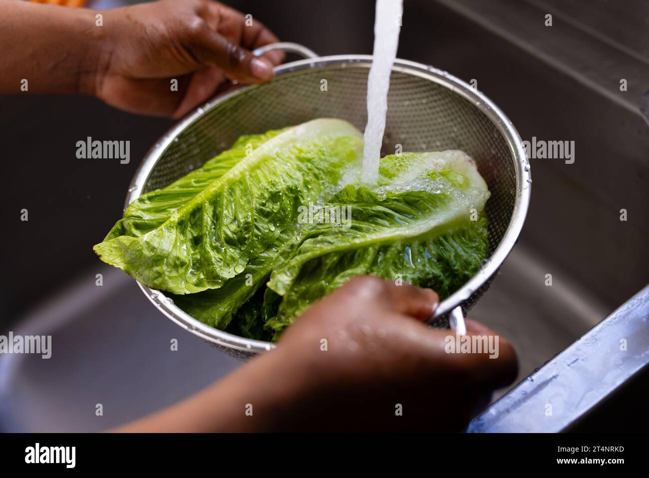 African american male chef washing vegetables in sink in restaurant ...