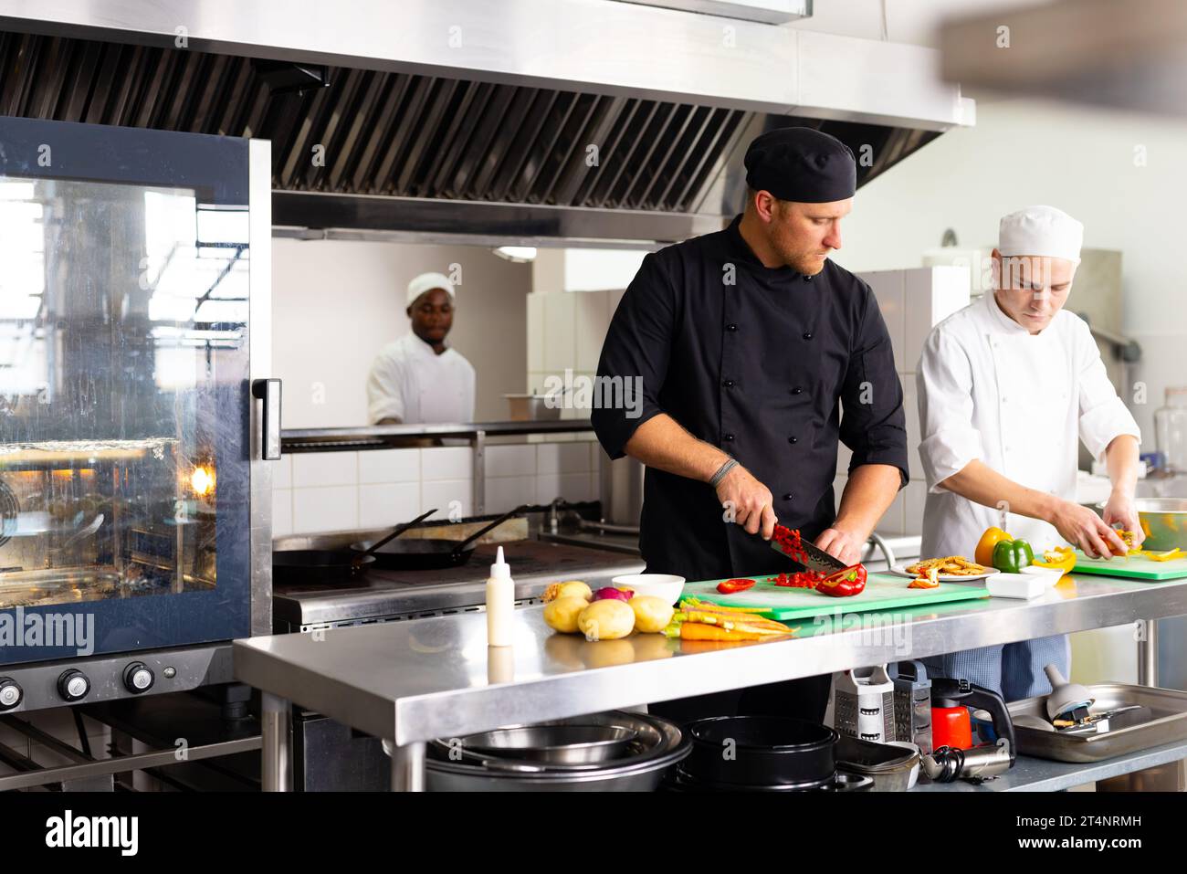 Three diverse male chefs cutting vegetables and cooking in restaurant ...
