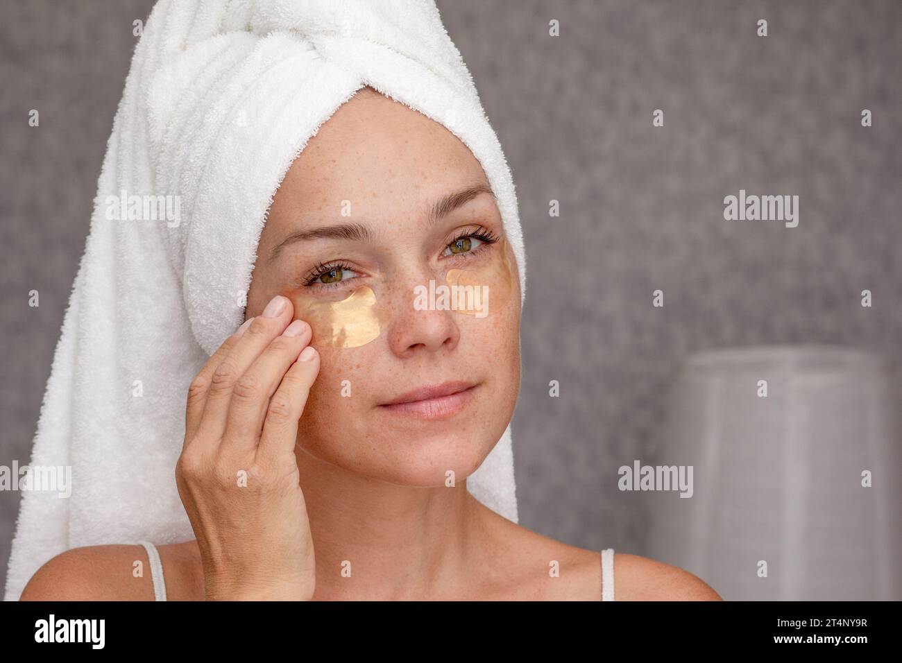 Woman of 40s after shower with towel on head with gold patches under ...