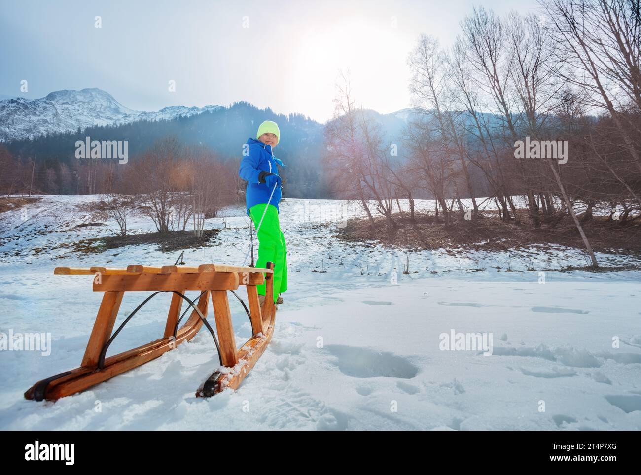 Boy in winter outfit pull wooden sledge uphill turning back Stock Photo ...
