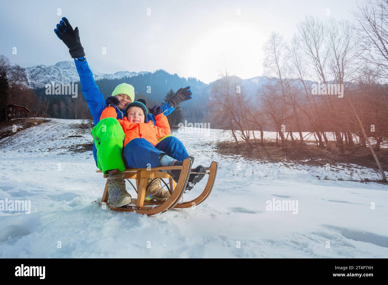Two boys going downhill on wooded sledge lift hands and have fun Stock ...