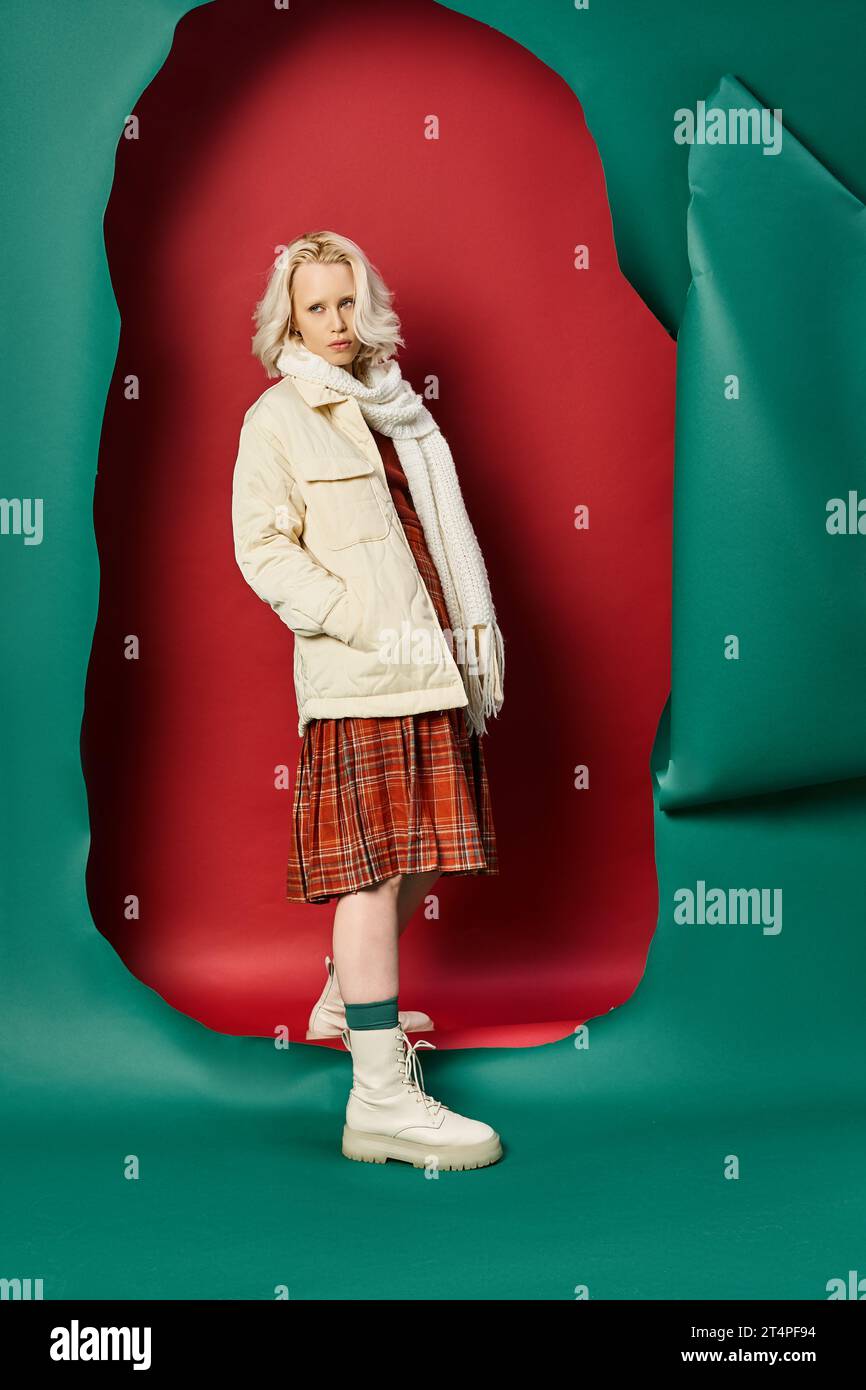 full length of blonde woman in stylish winter outfit posing on red with ...