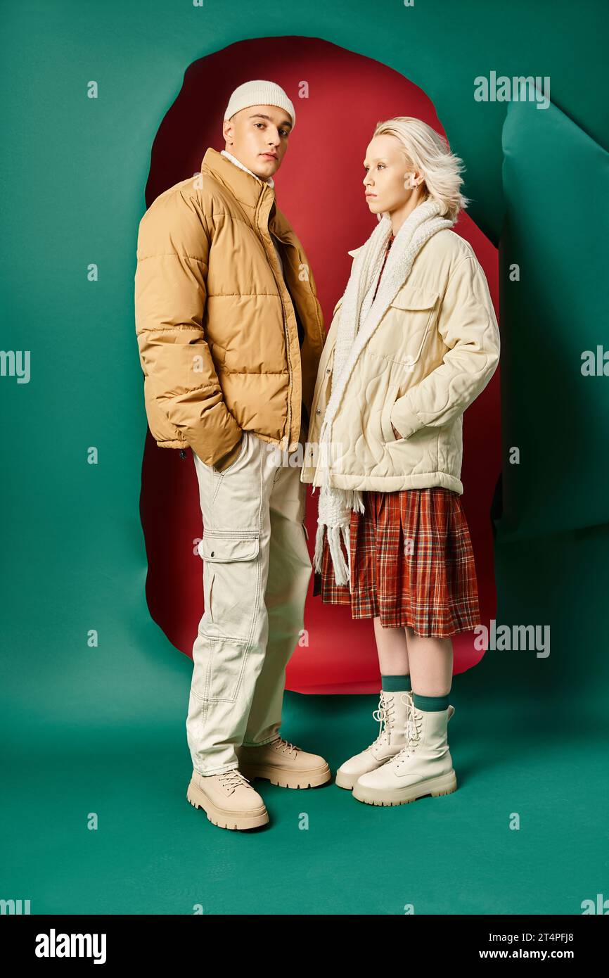 full length of couple in modern winter jackets posing together on red ...