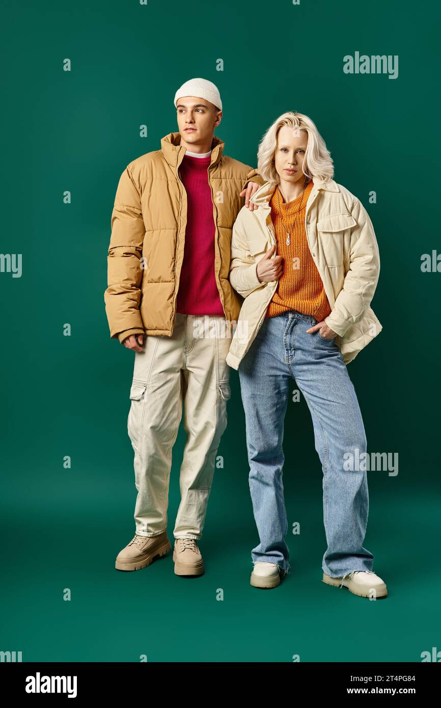 couple in winter puffer jackets posing together on turquoise background ...