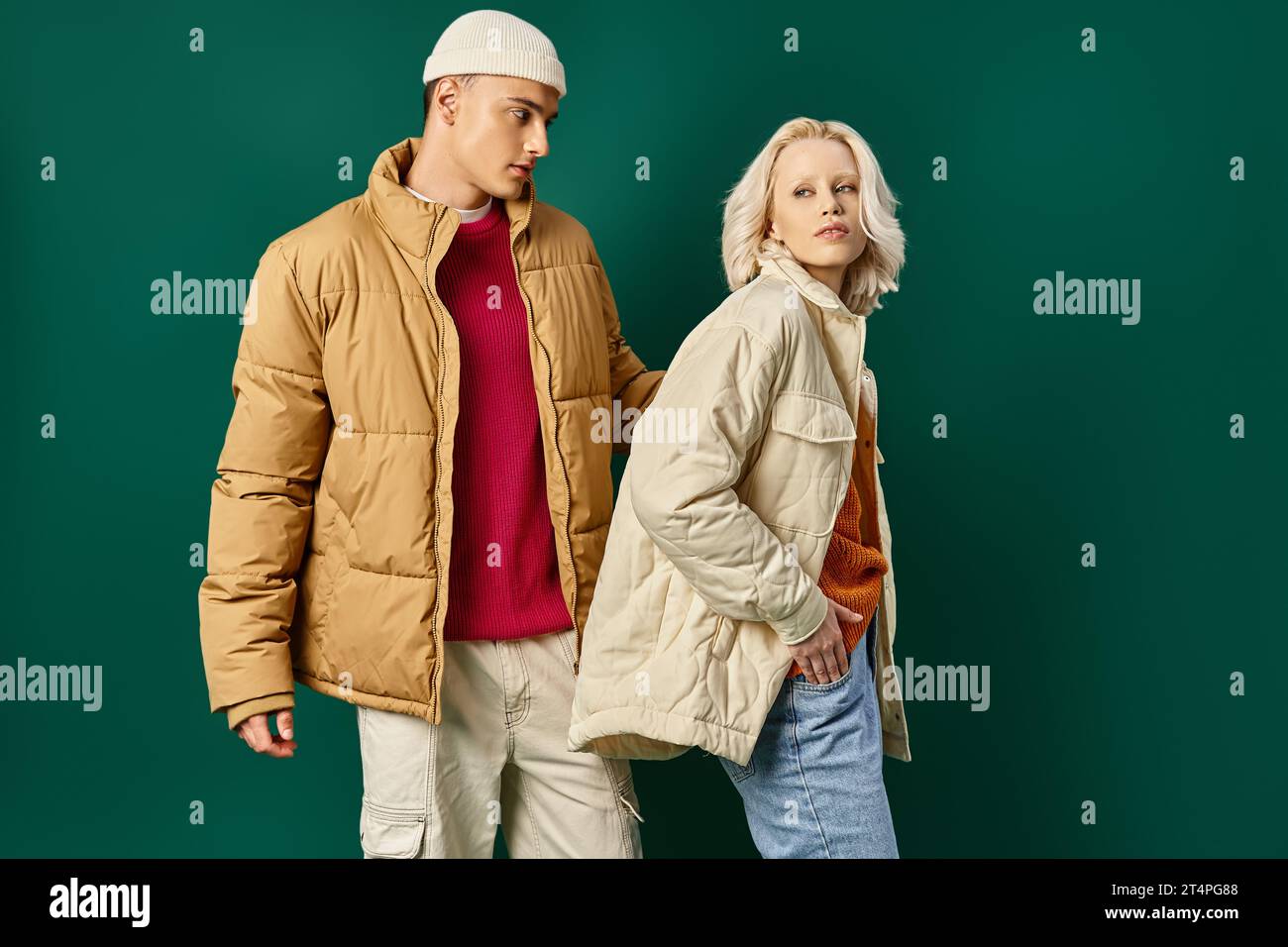 young couple in puffer jackets posing together on turquoise background ...