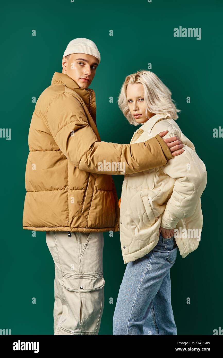 stylish couple in puffer jackets posing together on turquoise ...